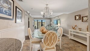 Uma sala de jantar com mesa de vidro, cadeiras brancas e um candelabro.