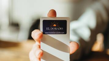 Uma mão segurando um cartão de visita com o texto 'EL DORADO' e um endereço de site.