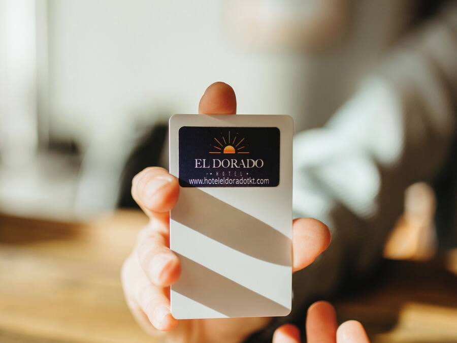 Uma mão segurando um cartão de visita com o texto 'EL DORADO' e um endereço de site.