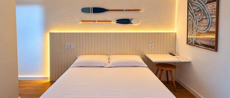 Quarto de hotel com cama, escrivaninha e dois remo no muro.