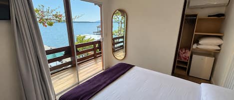 Quarto com cama, guarda-roupa, espelho e vista para o mar através de uma porta de correr.