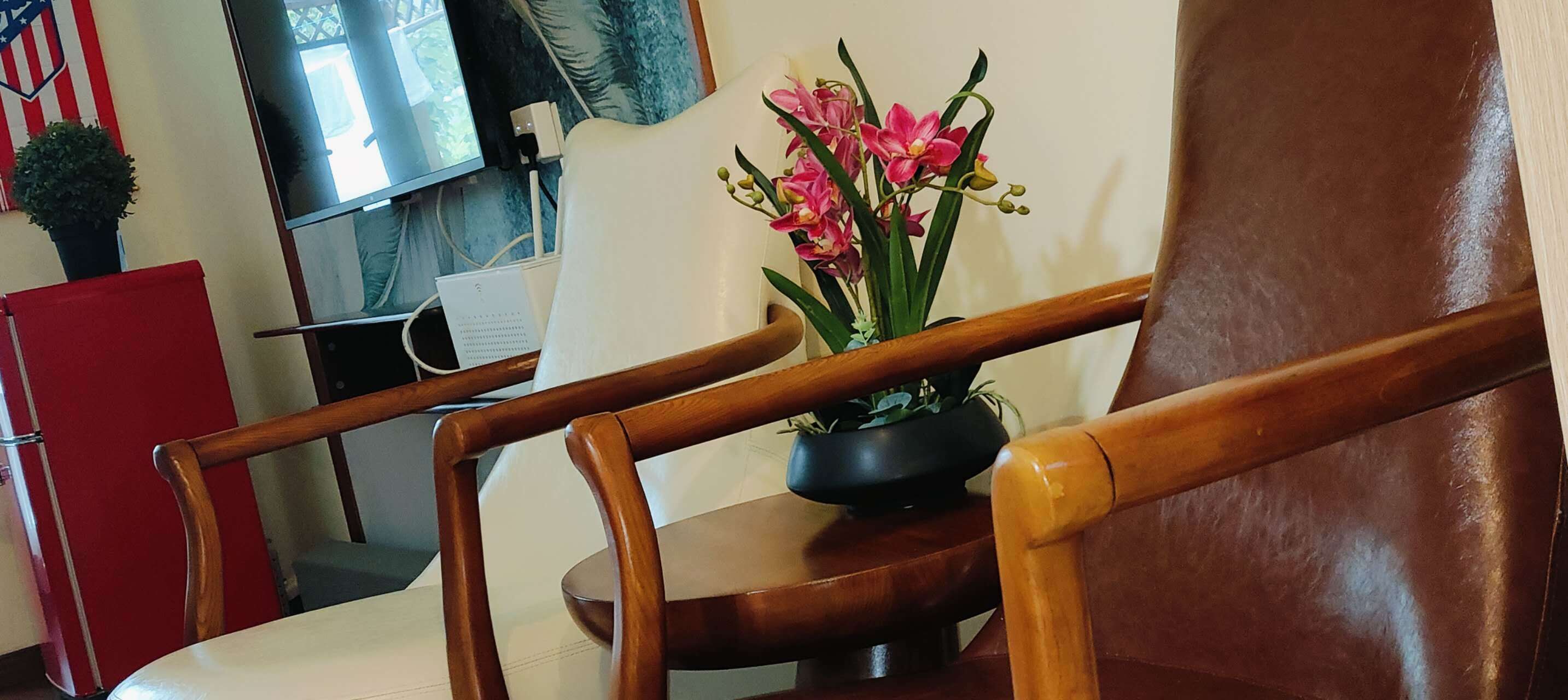 Uma cadeira de madeira com um vaso preto de flores cor-de-rosa sobre uma mesa.
