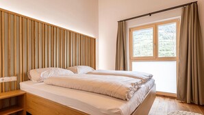 Quarto com cabeceira de madeira, cama com roupa de cama branca, mesa de cabeceira e janela com cortinas.