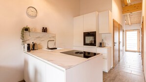 Uma cozinha moderna com armários brancos, bancada de mármore, forno embutido e um relógio na parede.