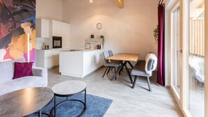 Uma cozinha moderna com armários brancos, uma ilha central e um espaço de jantar com mesa e cadeiras de madeira.