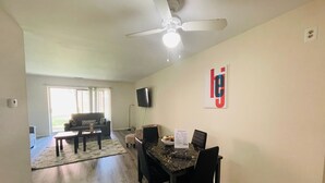 Uma sala de jantar com uma mesa, cadeiras, um ventilador de teto e uma televisão na parede.