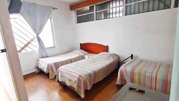 Quarto em dormitório com duas camas de solteiro, uma mesa pequena e uma janela com cortinas.
