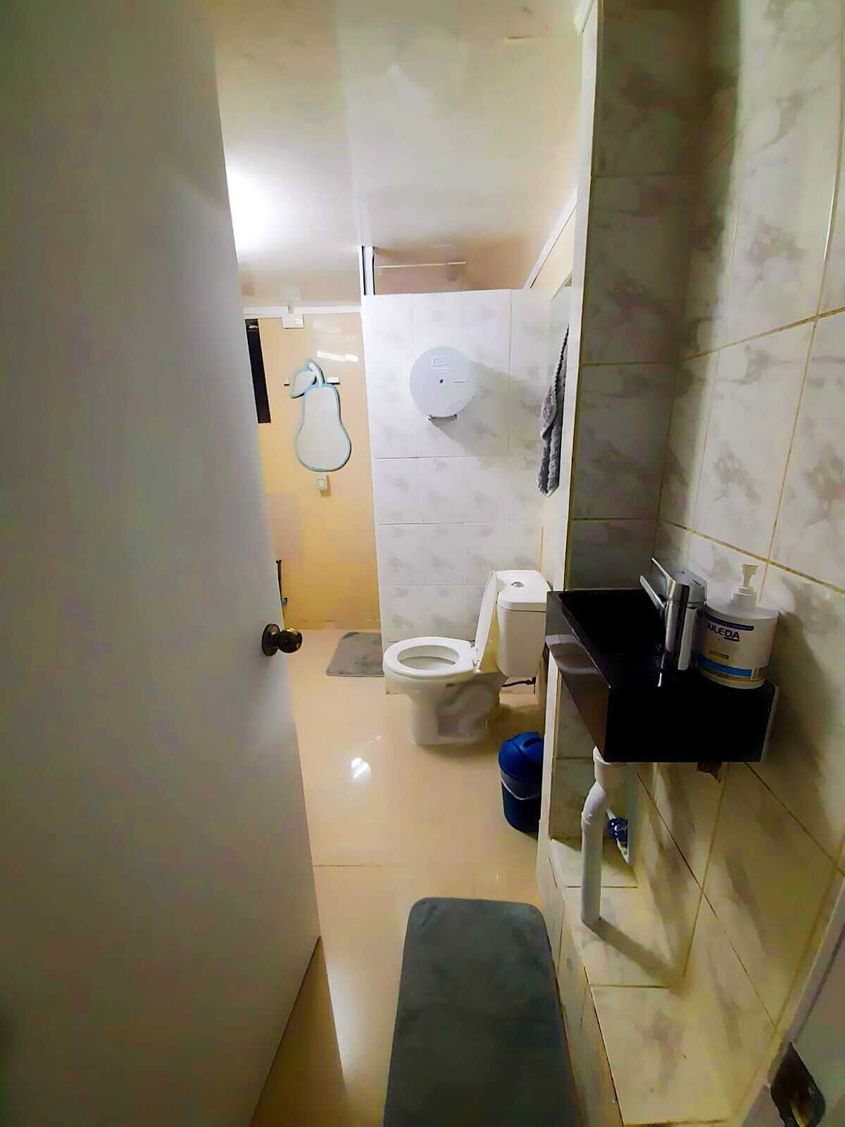 Casa de banho compacta com sanita, zona de duche e lavatório com dispensador de sabonete.