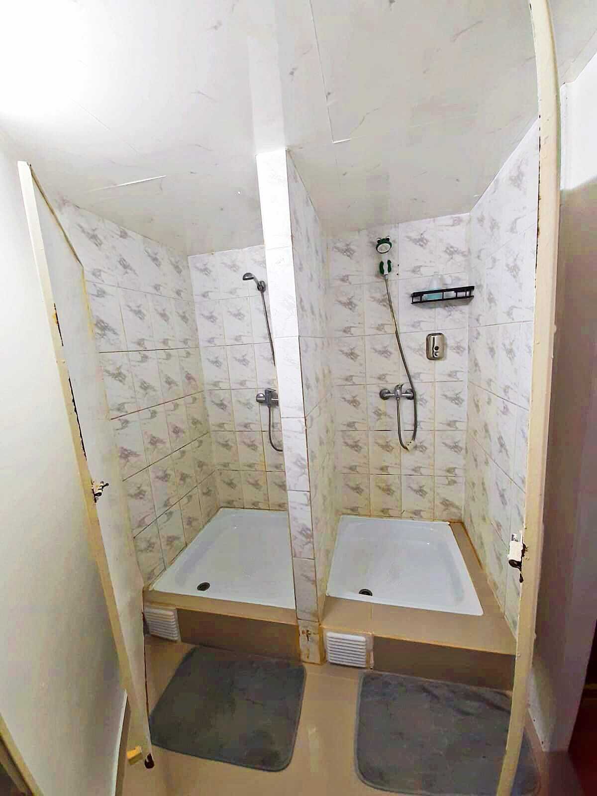 Uma casa de banho com dois chuveiros separados, cada um com banheira, chuveiro manual e torneira fixa na parede.