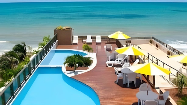 Área da piscina com vista para o oceano, mobiliário de exterior e guarda-sóis.