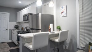 Cozinha moderna com armários brancos, eletrodomésticos de aço inoxidável e um espaço bar com cadeiras brancas.