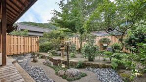 Um jardim japonês tradicional com estruturas de madeira, um caminho de cascalho e diversas plantas.