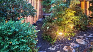 Uma casa japonesa tradicional com fachada de madeira, telhado de telhas e um jardim com caminho de pedra e vegetação.