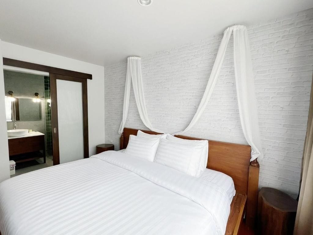 Quarto de hotel com uma cama grande, cabeceira de madeira e parede de tijolos brancos.