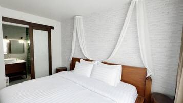 Quarto de hotel com uma cama grande, cabeceira de madeira e parede de tijolos brancos.