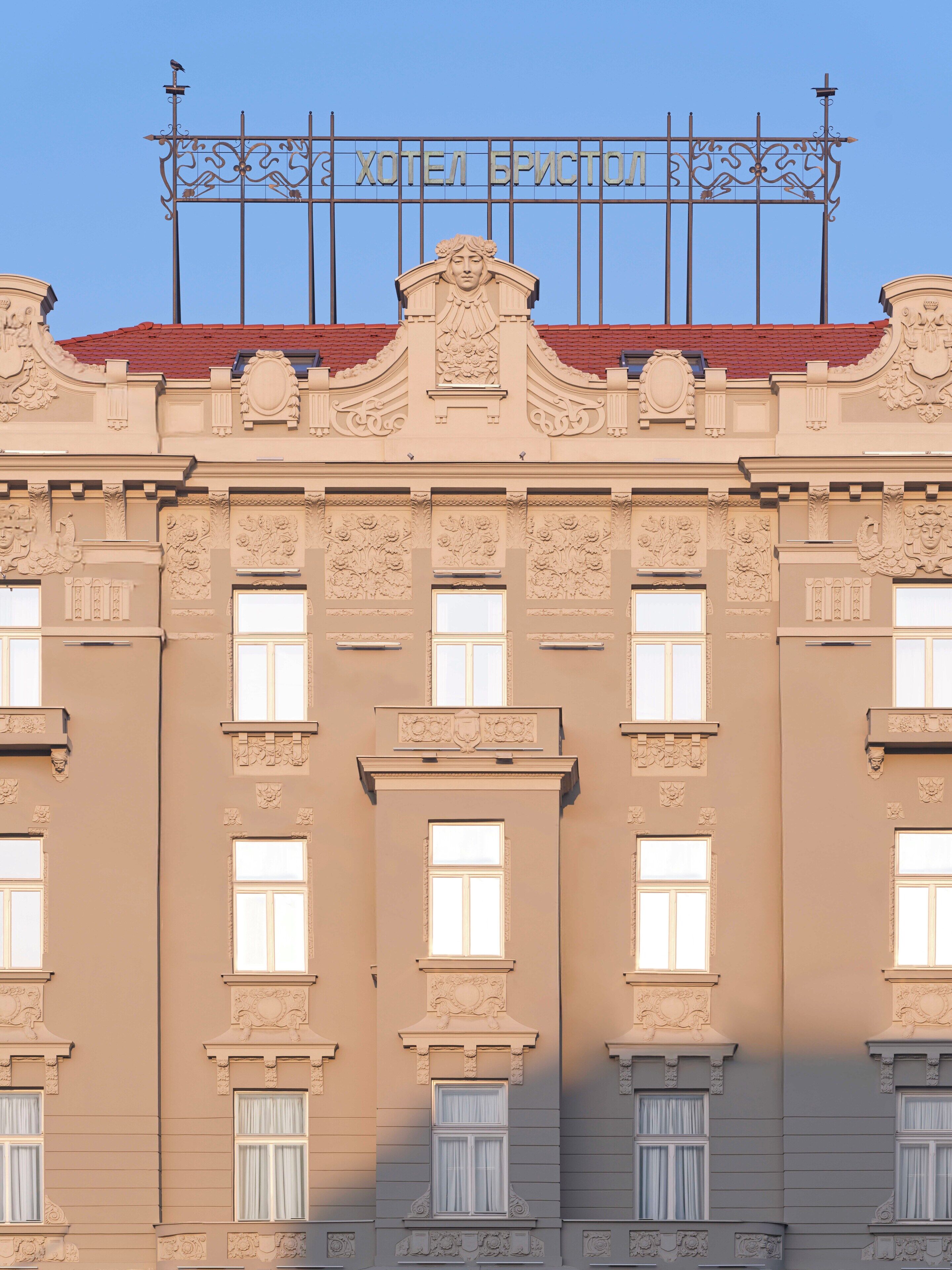 Um edifício com detalhes arquitetônicos elaborados, incluindo uma placa de metal decorativa sobre a entrada e várias janelas com molduras brancas.