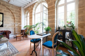 Um quarto com uma mesa, cadeiras, uma estante e grandes janelas.