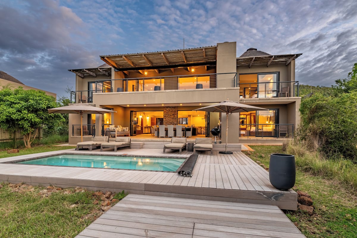 Uma casa moderna de dois andares com piscina, área de estar externa e um pátio.