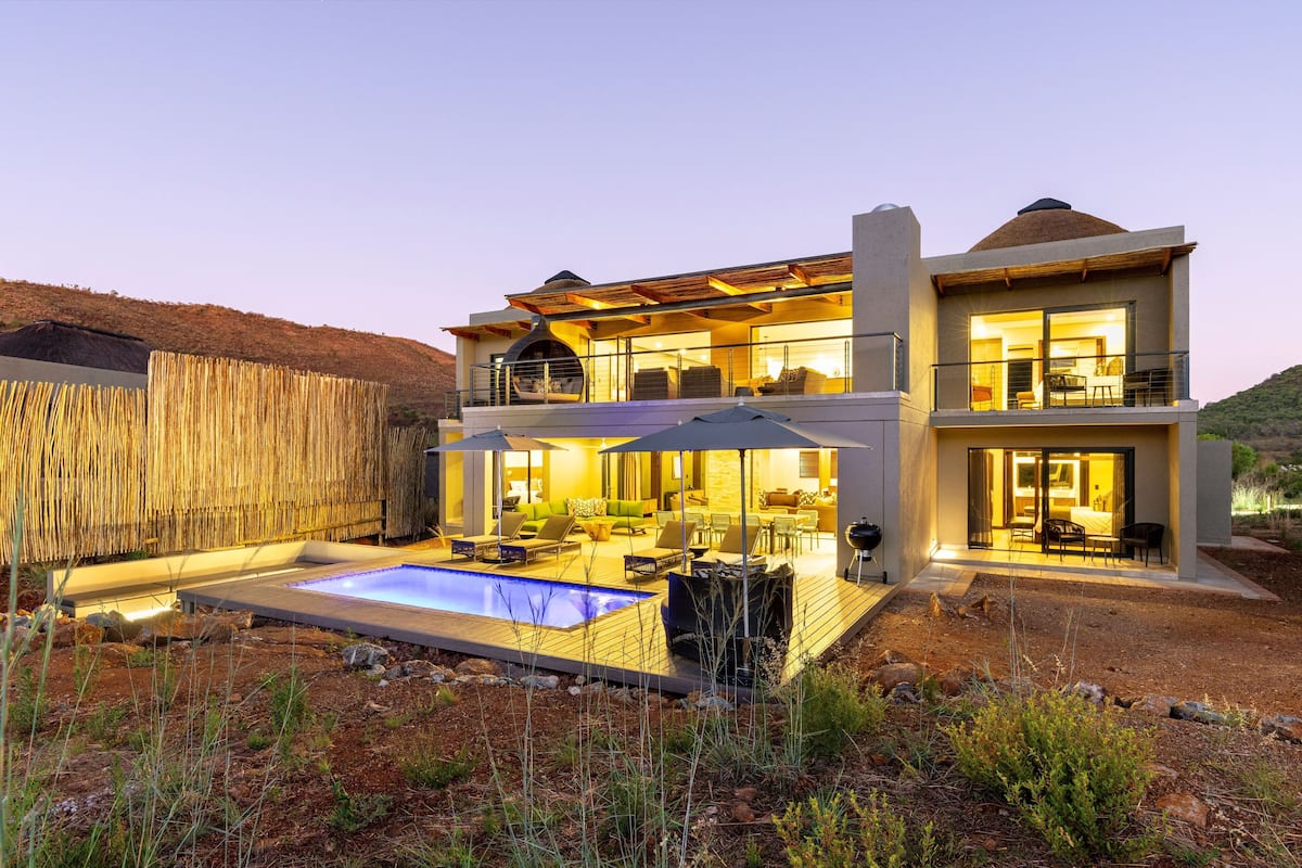 Uma casa de dois andares com piscina, área de estar externa e uma varanda grande.