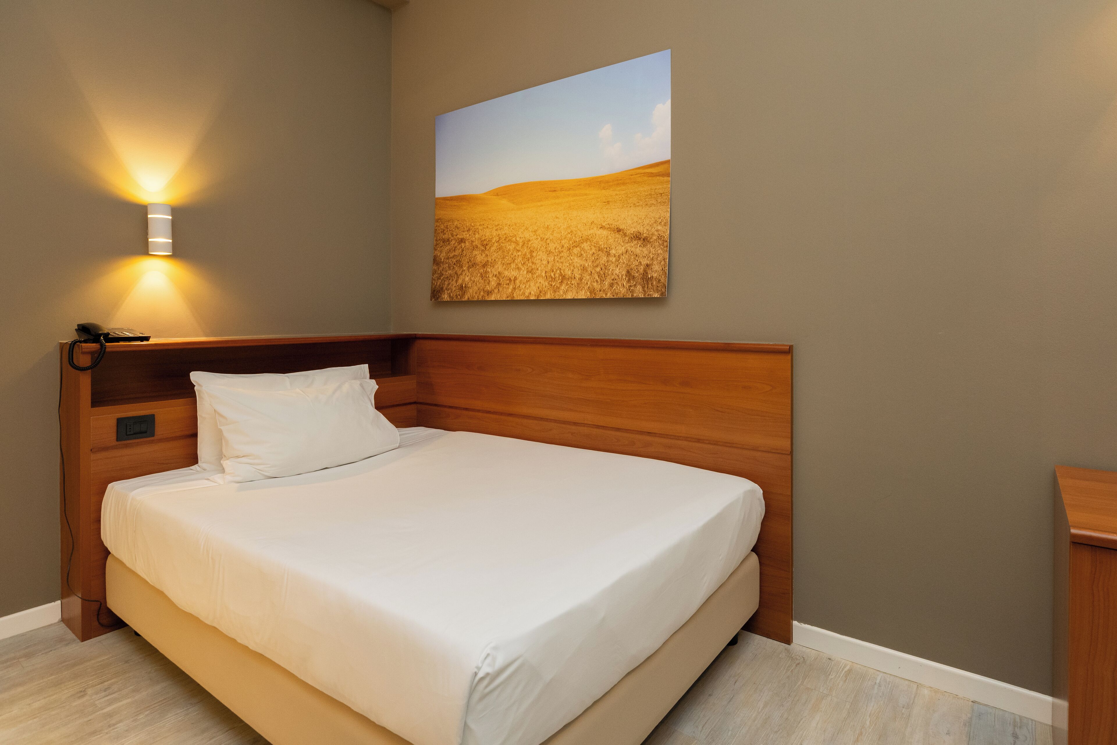 Uma cama bem arrumada com cabeceira de madeira, um abajur e um quadro de uma paisagem na parede.