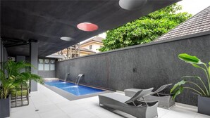 Uma área de piscina moderna ao ar livre, com hidromassagem integrada, espreguiçadeiras e plantas em vasos.