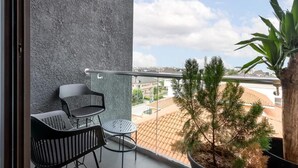 Varanda com uma mesa pequena, duas cadeiras, um vaso de planta e vista para a cidade.