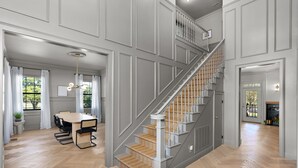Um quarto espaçoso com piso de madeira em padrão herringbone, uma área de refeições com mesa e cadeiras, e uma escada com corrimão.