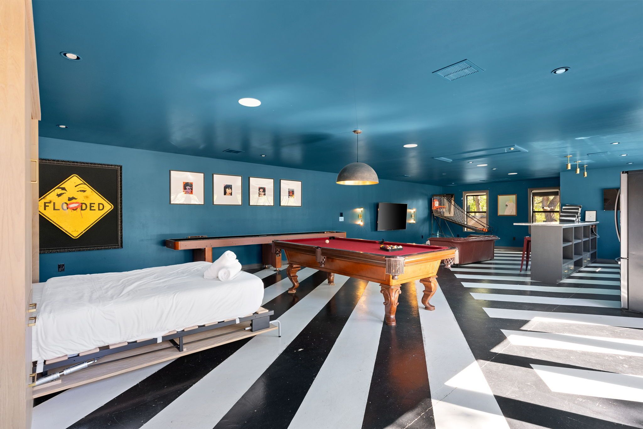 Quarto com mesa de bilhar, cama, área de bar e parede azul com uma placa que diz 'inundado'.