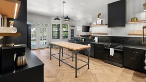Uma cozinha moderna com armários pretos, uma mesa de madeira e iluminação pendente.