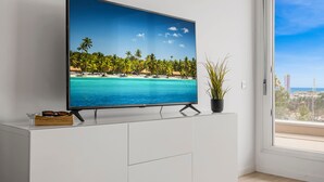 Uma TV de tela plana sobre um armário branco, exibindo uma paisagem praiana tropical.