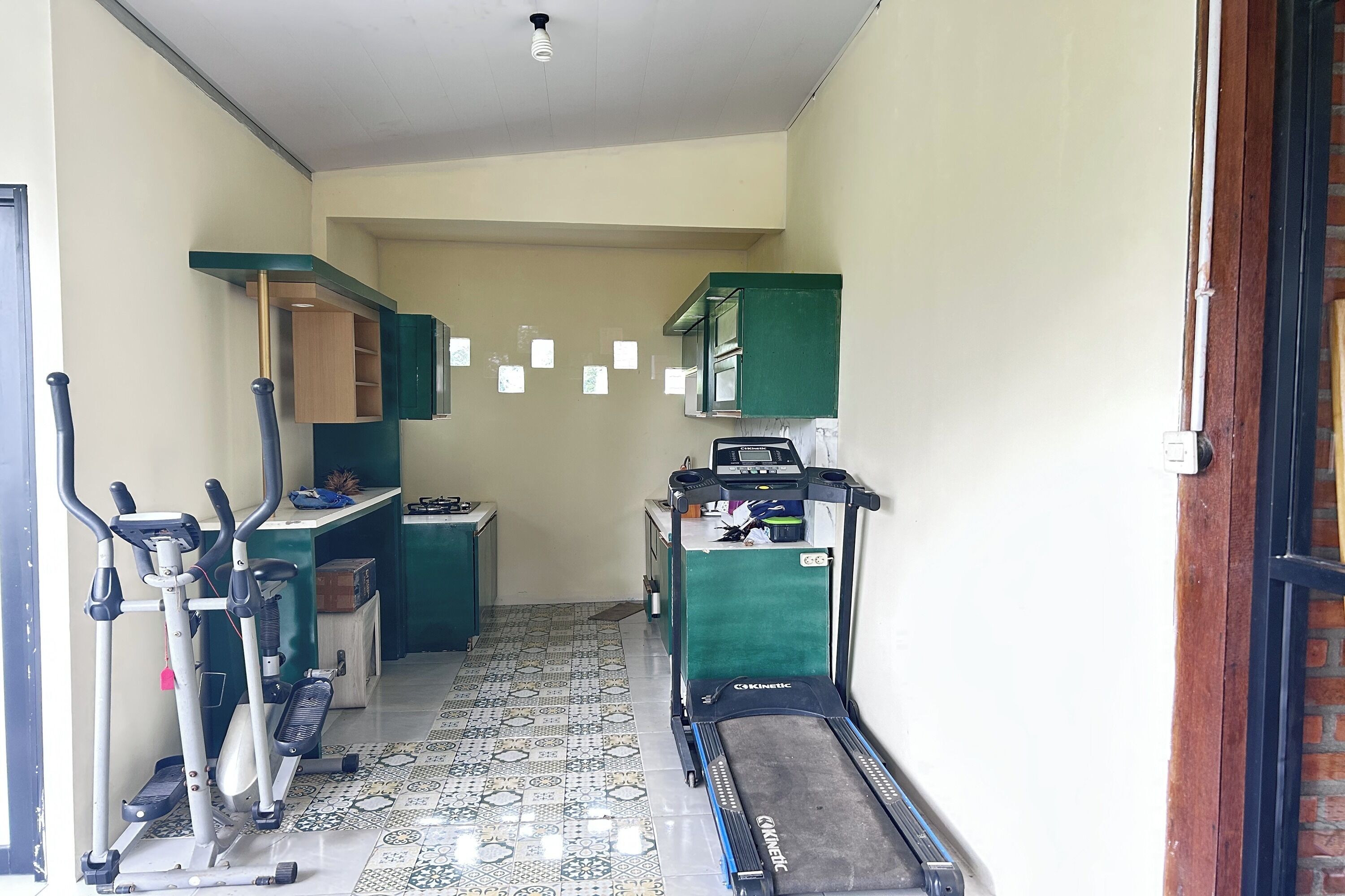 Corredor com equipamentos de ginástica, incluindo esteiras e elípticos, que leva a uma cozinha com armários e bancada.