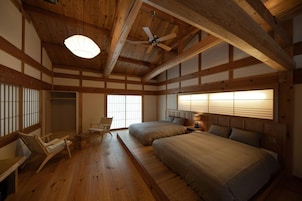 Um quarto tradicional em estilo japonês, com piso de tatame, teto baixo com vigas aparentes, ventoinha de teto e janela com tela shoji.