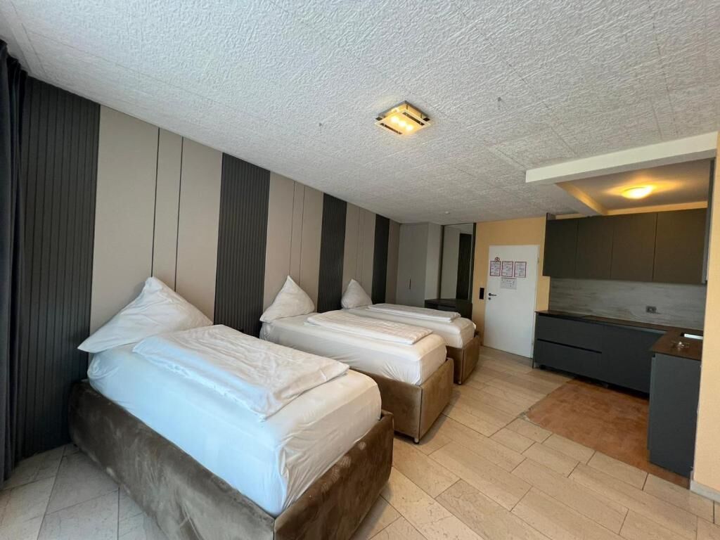 Quarto de hotel com duas camas, uma cozinha compacta e um banheiro.