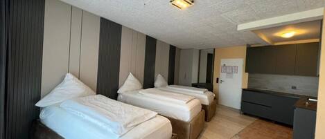 Quarto de hotel com duas camas, uma cozinha compacta e um banheiro.