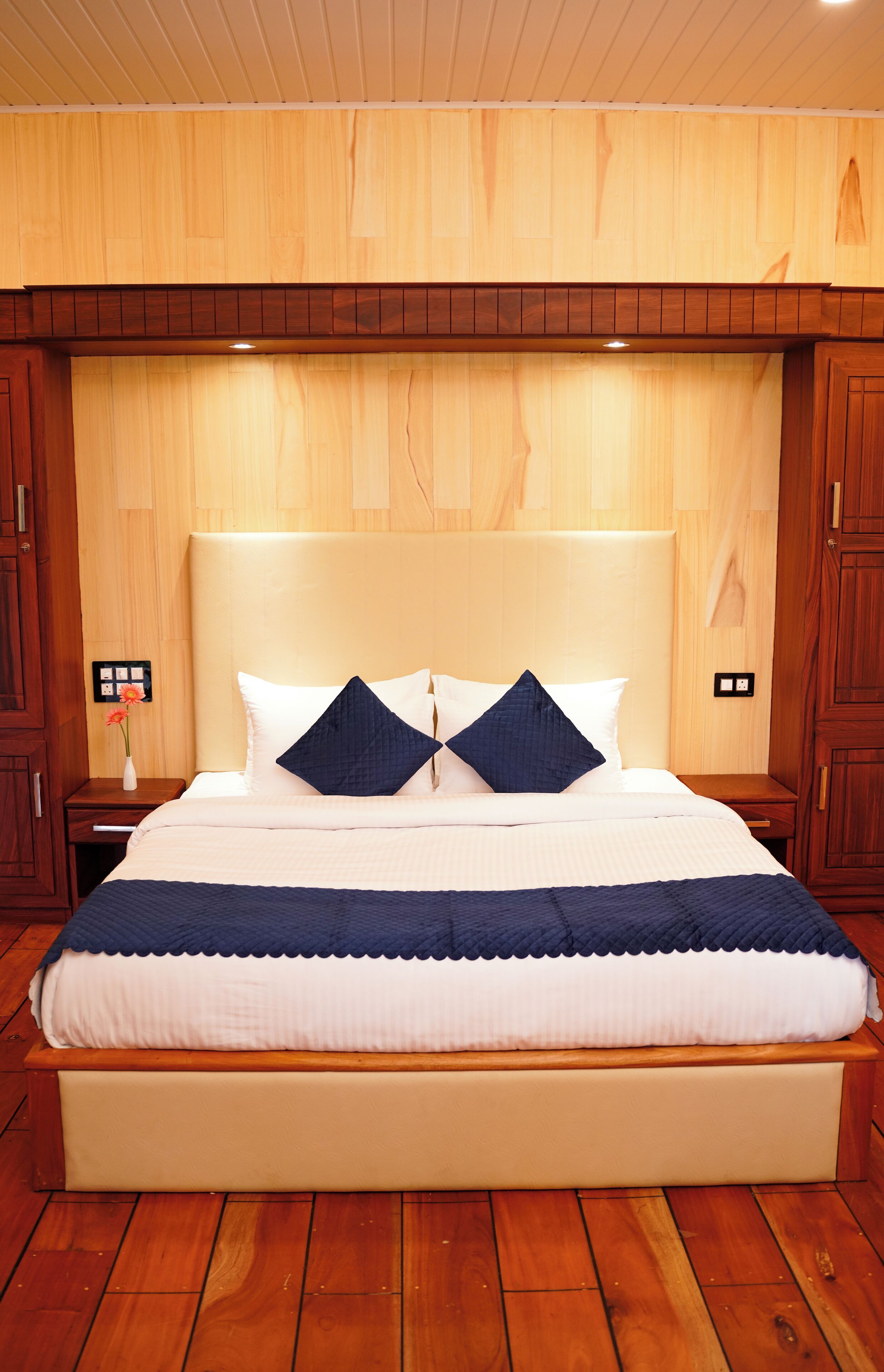 Uma cama grande com cabeceira de madeira, duas mesas de cabeceira e chão de madeira.