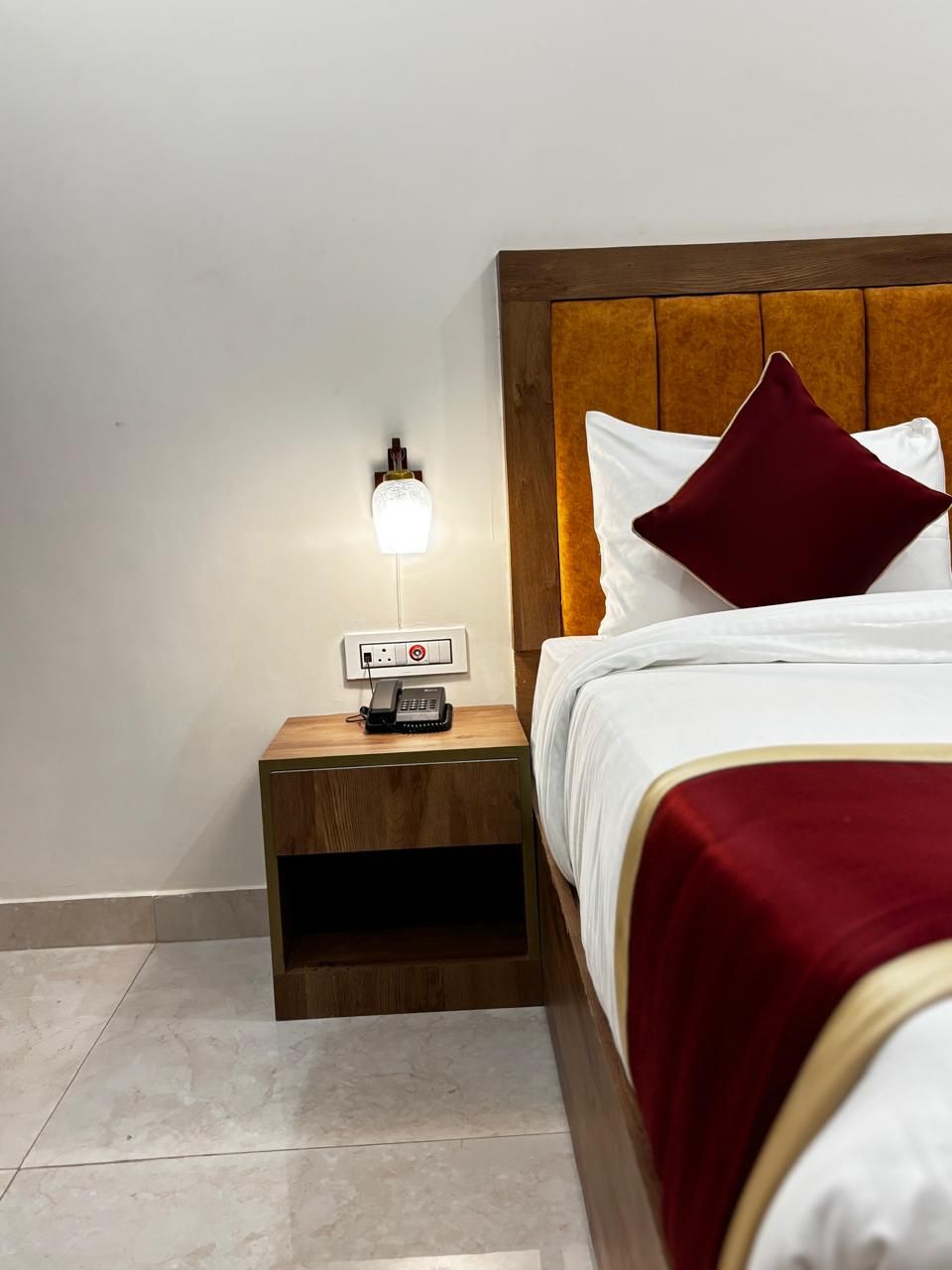 Quarto de hotel com cabeceira de madeira, mesa de cabeceira com abajur e telefone.