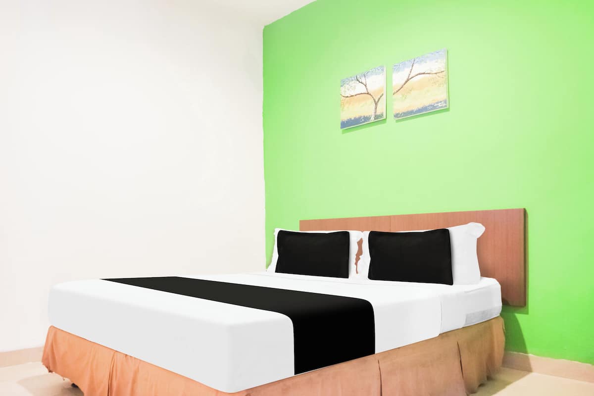 Quarto de hotel com cama, paredes verdes e duas pinturas na parede.