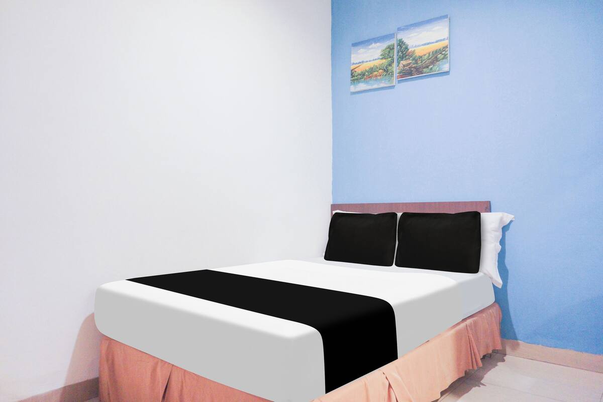 Uma cama com colcha preta e branca, saia de cama rosa e cabeceira com dois travesseiros pretos.