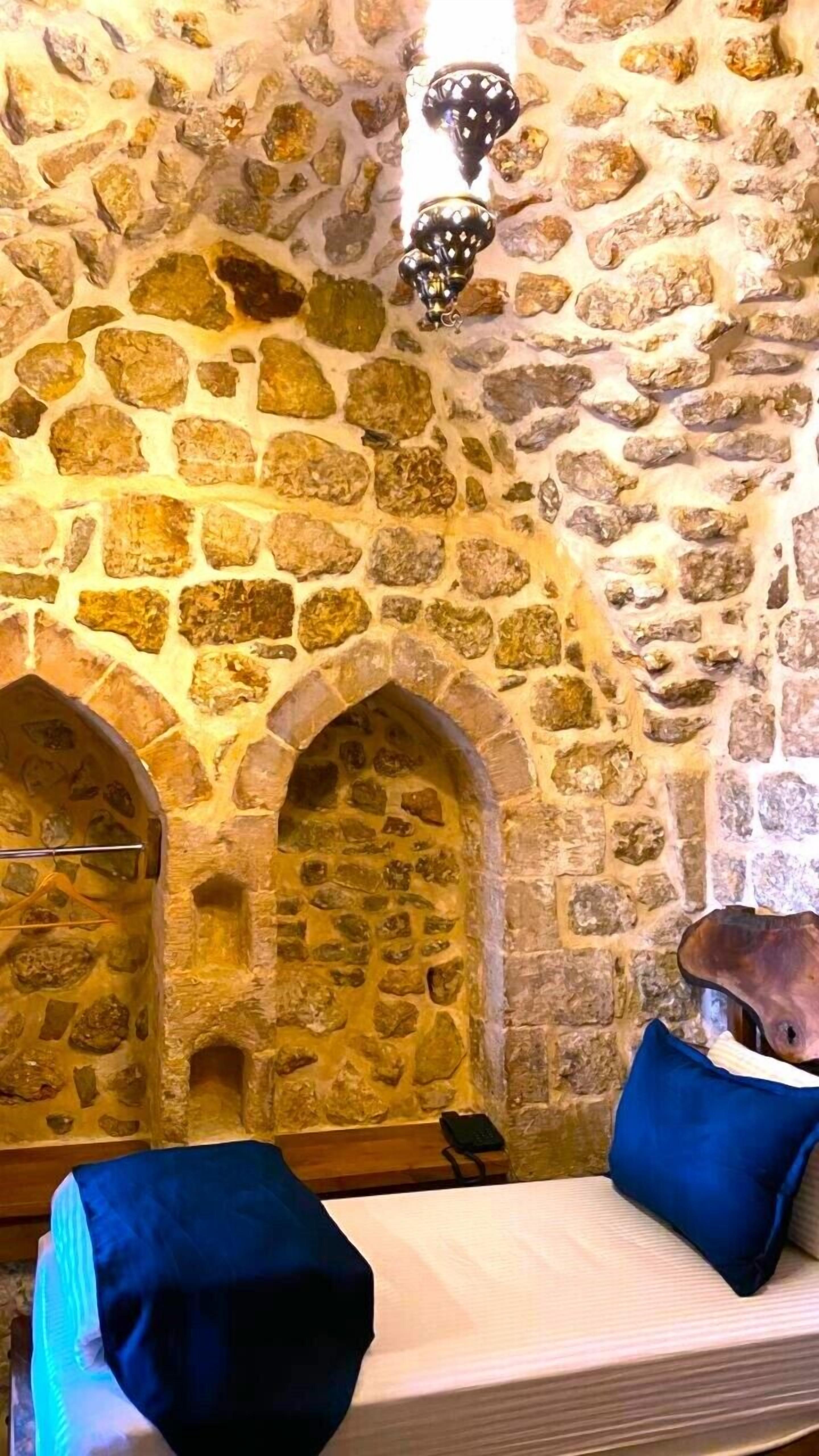 Quarto com paredes de pedra, duas alcovas em arco e uma cama com almofadas azuis.