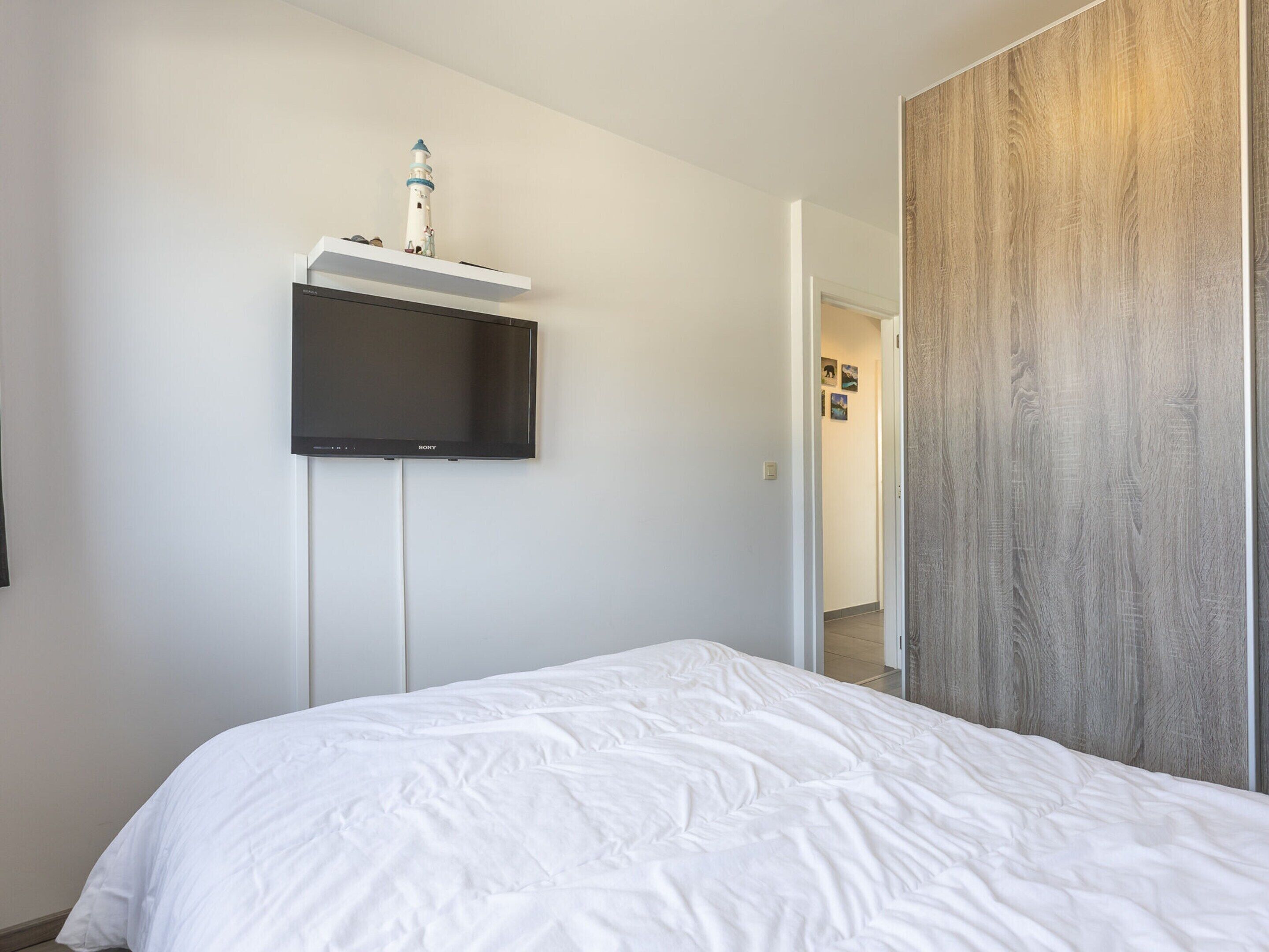 Quarto com cama, televisão na parede e guarda-roupa de madeira.