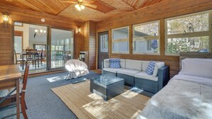 Interior de uma cabana de madeira com área de jantar, sofá e uma janela ampla.