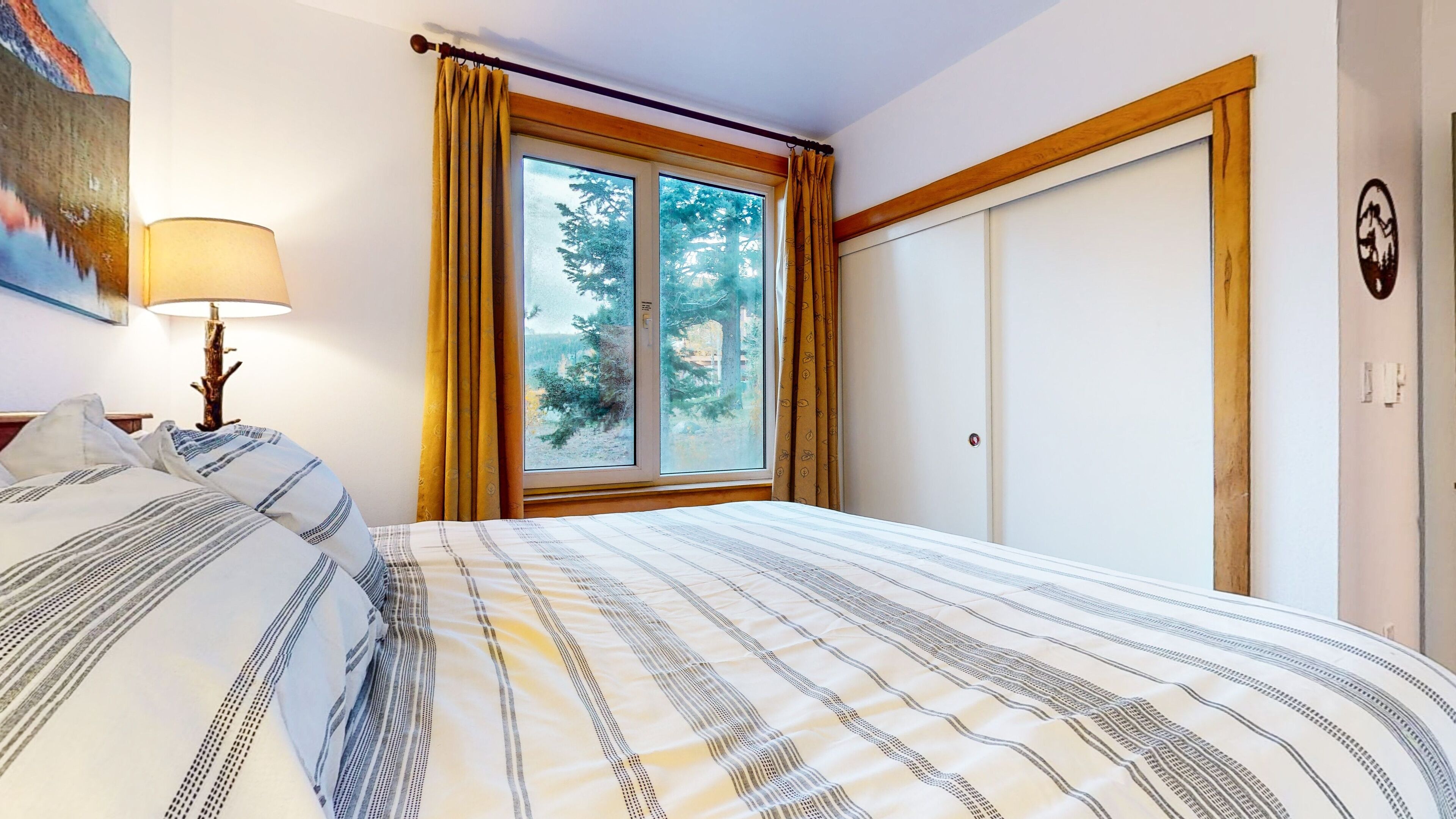 Quarto de hotel com cama, janela com cortinas, luminária e porta.