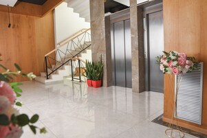 Um hall moderno com escada, elevadores e plantas em vasos.