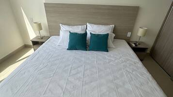 Cama bem arrumada com roupa de cama branca e dois travesseiros verde-água, uma cabeceira de madeira e duas obras de arte emolduradas acima.
