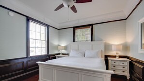 Quarto com cama grande, duas mesas de cabeceira com abajures, ventoinha no teto e janela com persianas.