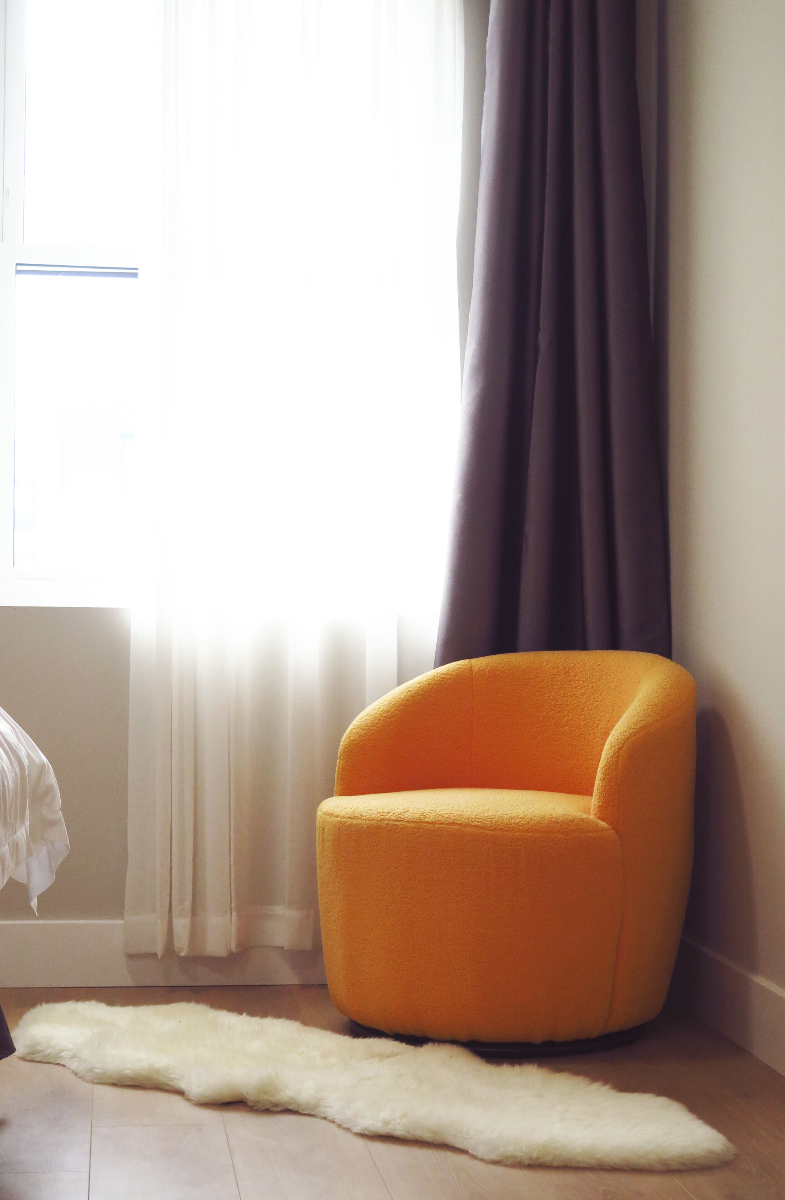 Quarto com poltrona amarela, tapete de pele branca e janela com cortinas.