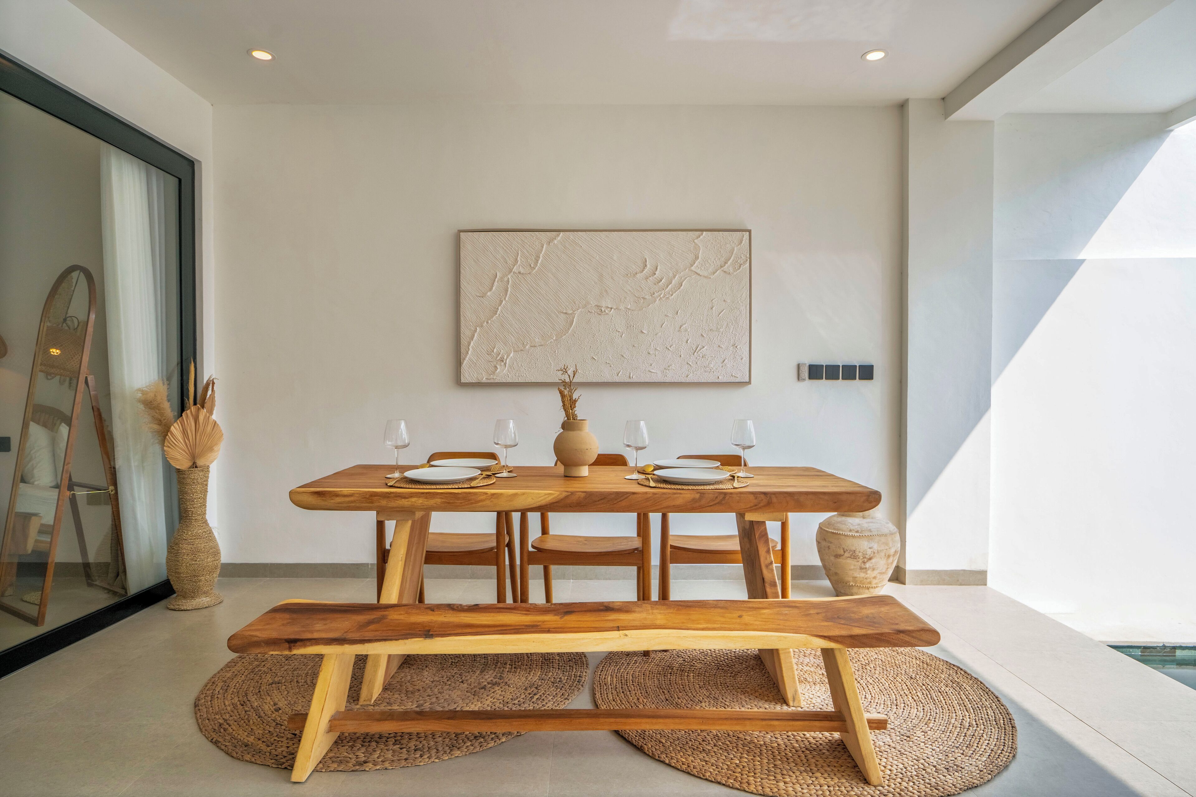 Uma sala de jantar moderna com uma mesa de madeira posta para quatro pessoas, cercada por tapetes trançados.