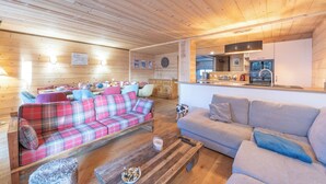 Interior acolhedor de uma cabana com teto de madeira, área de jantar com mesa e cadeiras, cozinha compacta e dois sofás.