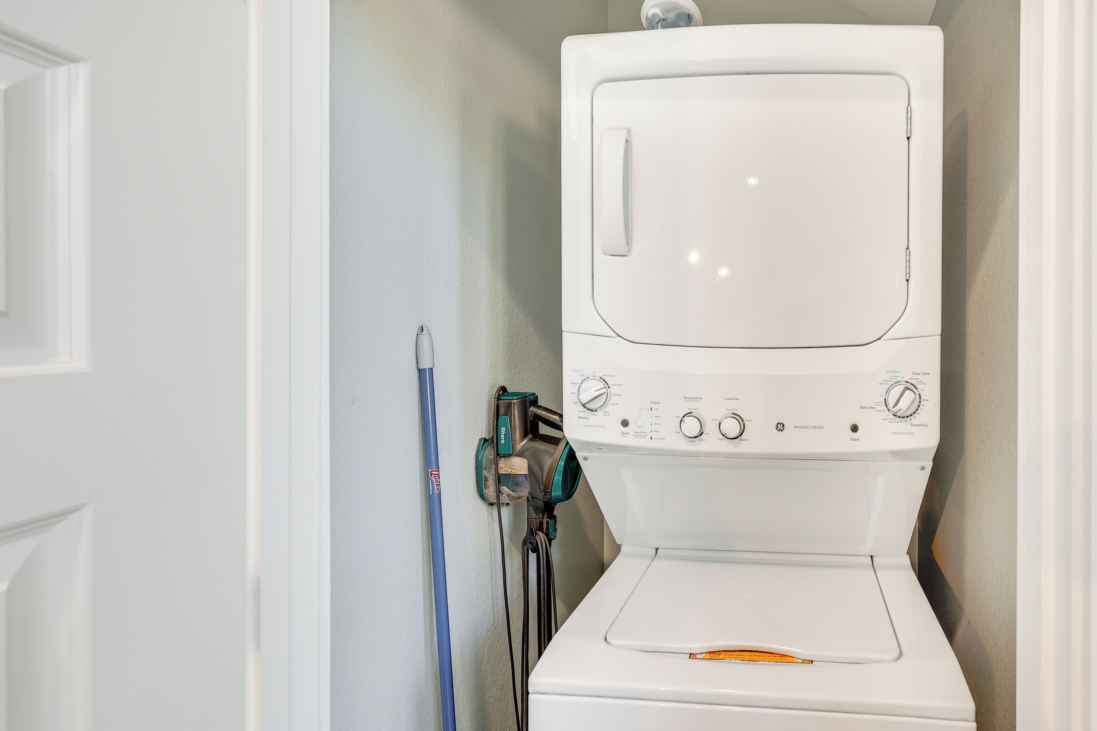 Máquina de lavar e secar de frente branca com botões de controle e visor digital, fixada na parede com uma porta por perto.