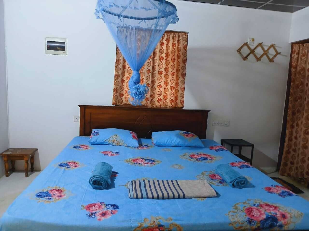 Quarto com cama, mesa de cabeceira, cortinas na janela e ar condicionado fixado na parede.